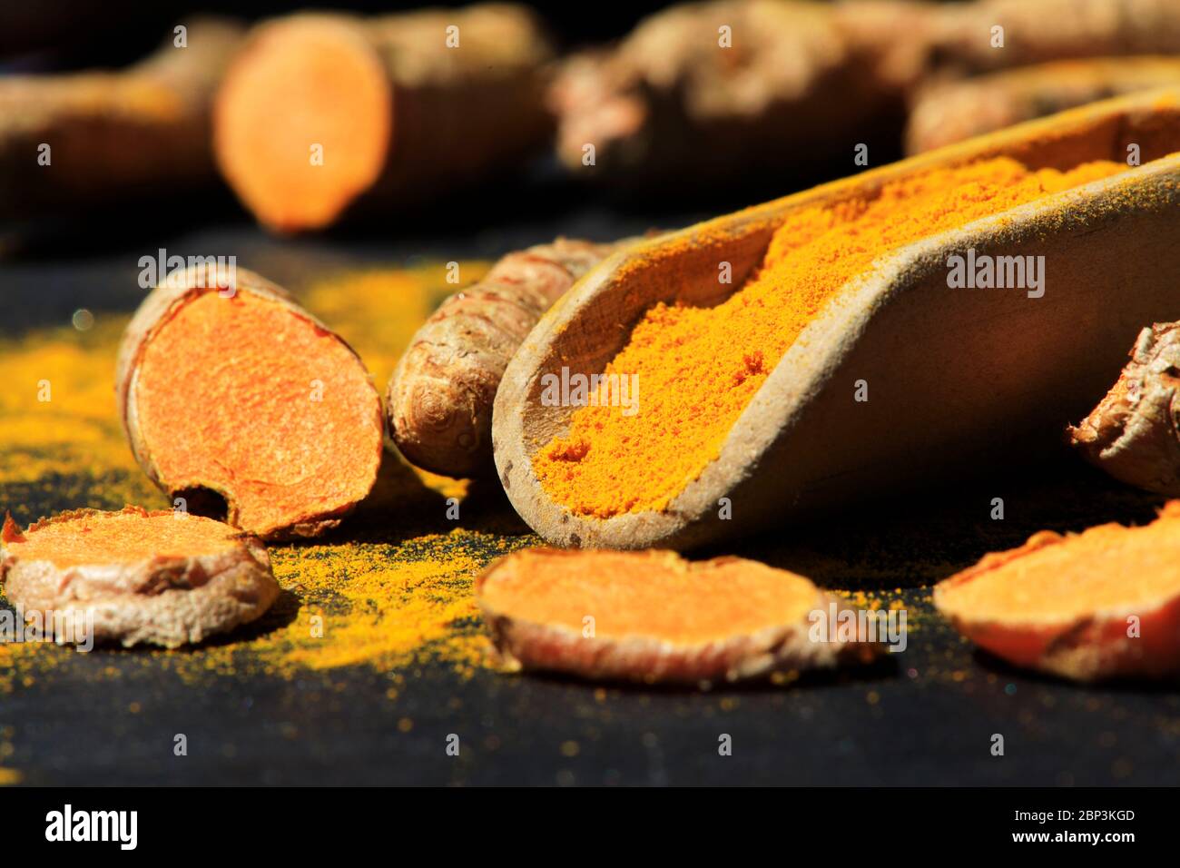 Turmeric powder (Kurkuma) in a wooden spoon and roots on a dark table ...