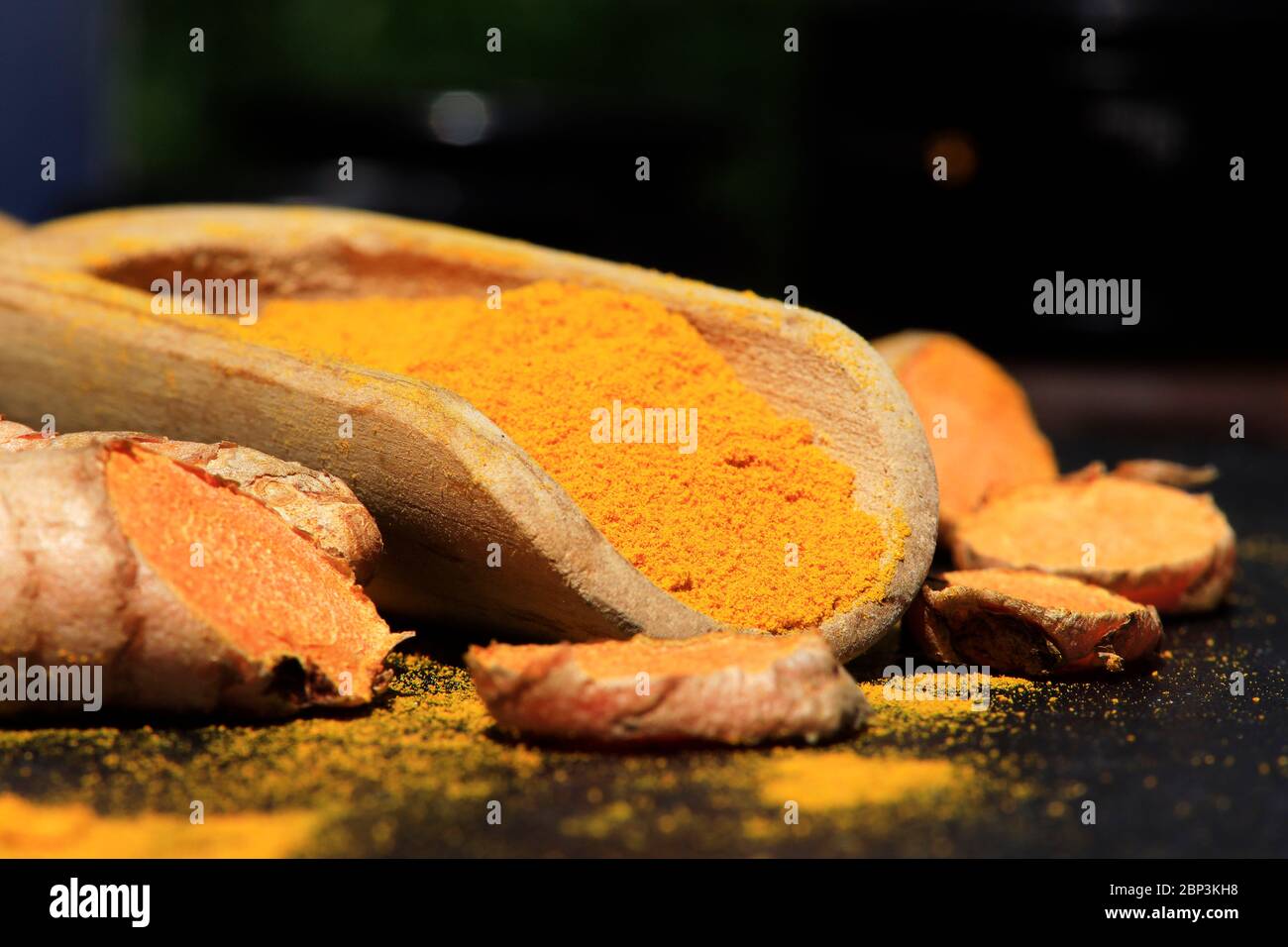 Turmeric powder (Kurkuma) in a wooden spoon and roots on a dark table ...