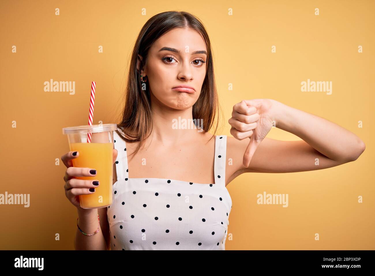 Young beautiful brunette woman drinking healthy orange juice over ...