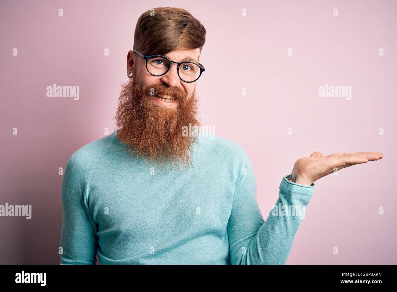 Handsome Irish redhead man with beard wearing glasses over pink ...
