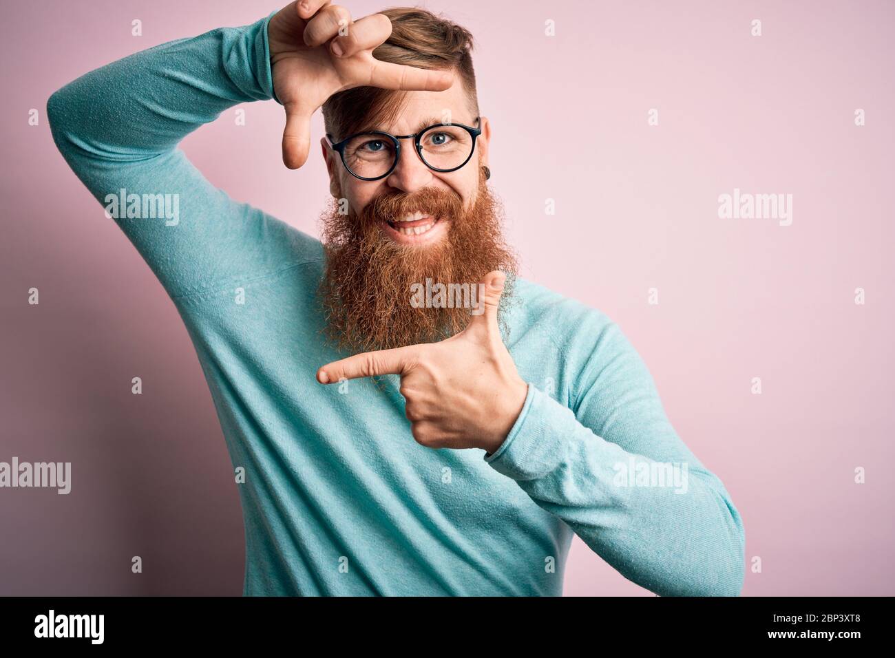 Handsome Irish redhead man with beard wearing glasses over pink ...