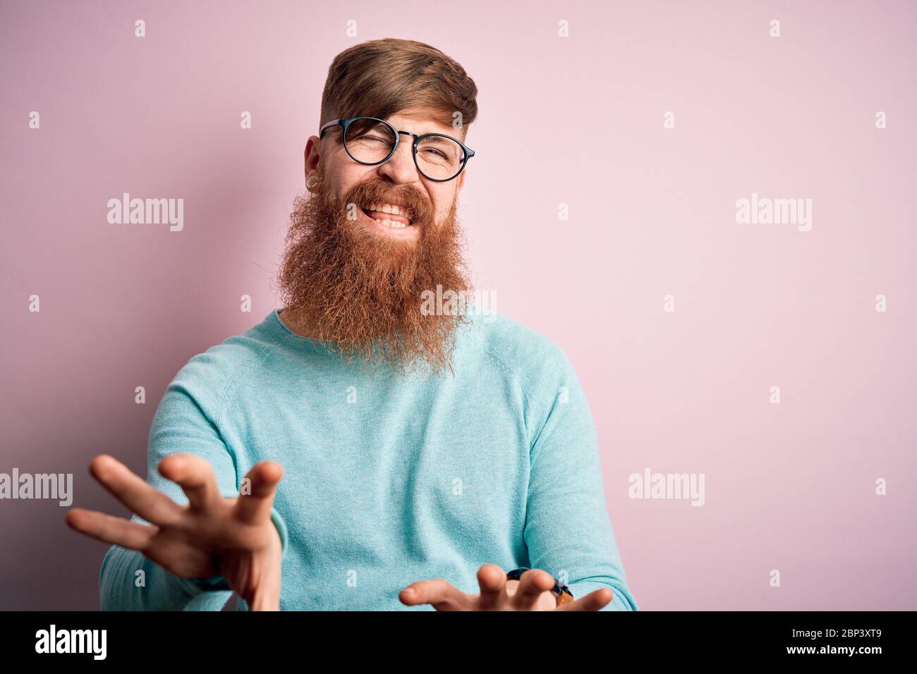 Handsome Irish redhead man with beard wearing glasses over pink ...