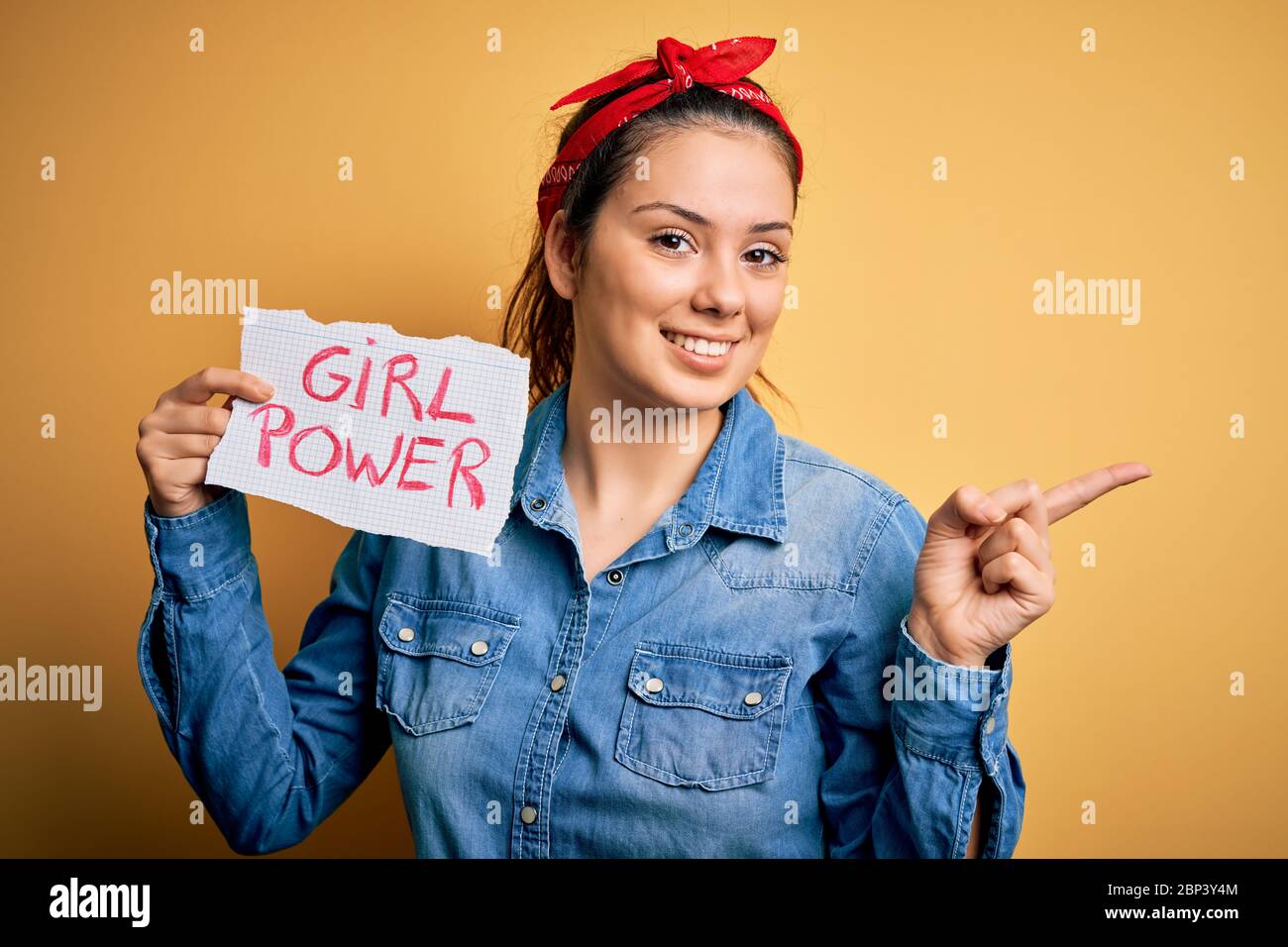 Young beautiful woman holding paper with girl power message over yellow ...