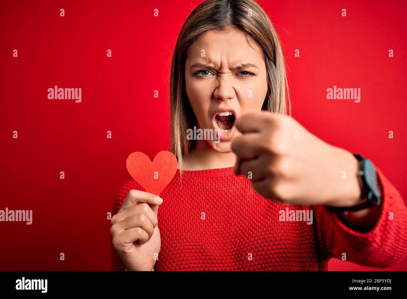 Young beautiful woman holding heart card standing over isolated red ...