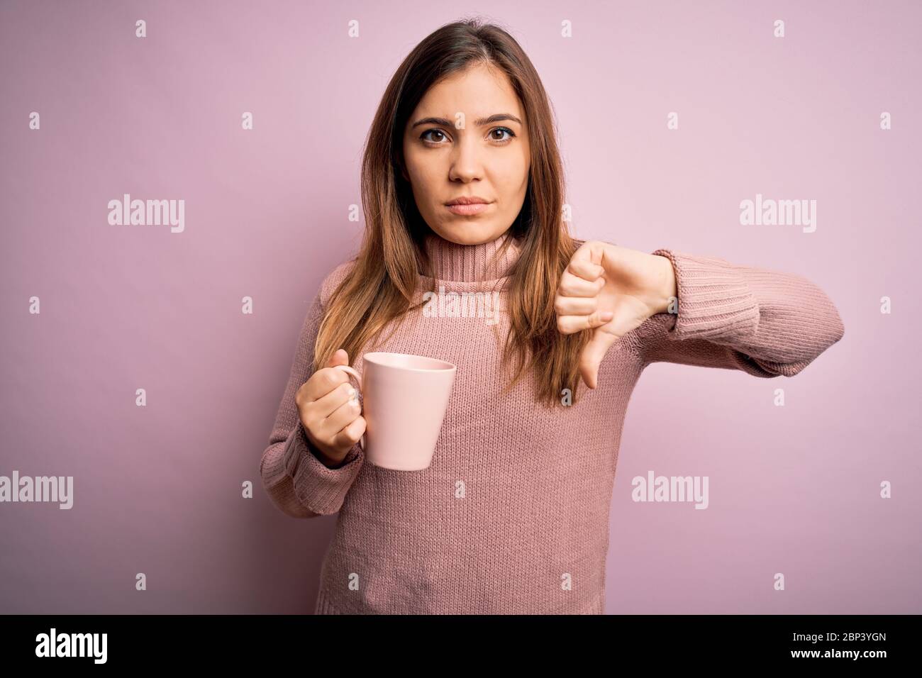 Young blonde woman drinking a cup of coffee over pink isolated background with angry face ...