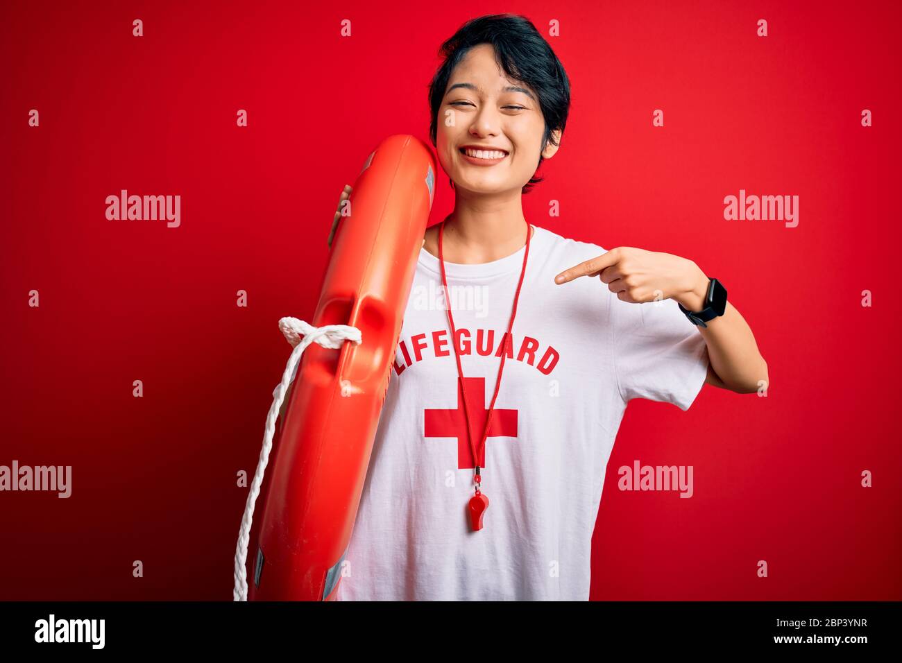 Young beautiful asian lifeguard girl using whistle holding orange float ...