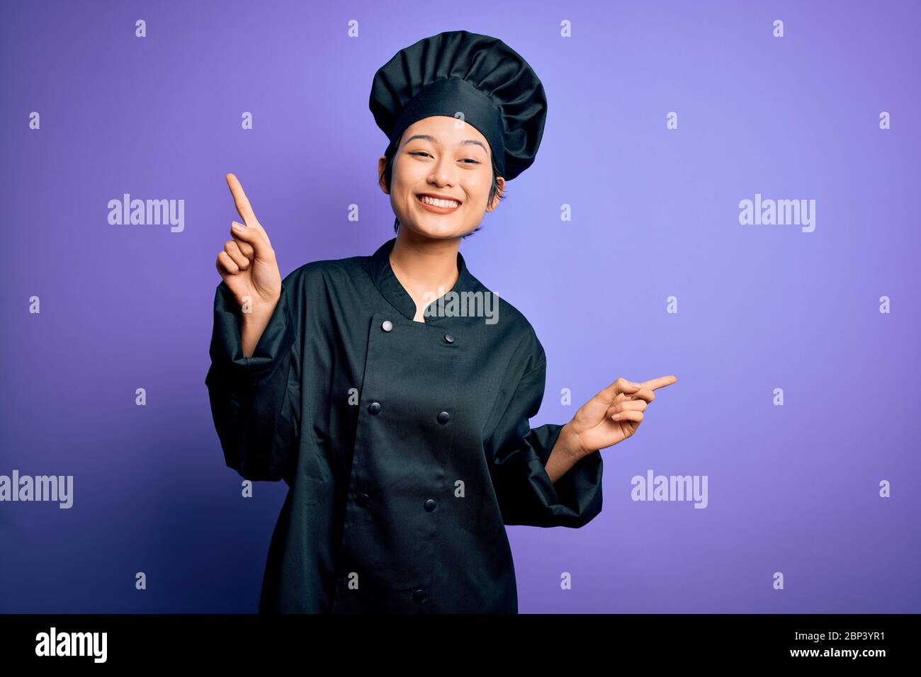 Young beautiful chinese chef woman wearing cooker uniform and hat over ...