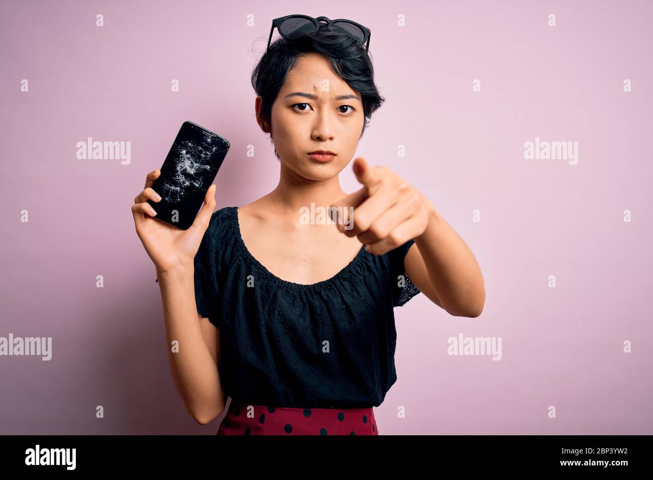 Young beautiful chinese woman holding broken smartphone showing craked ...