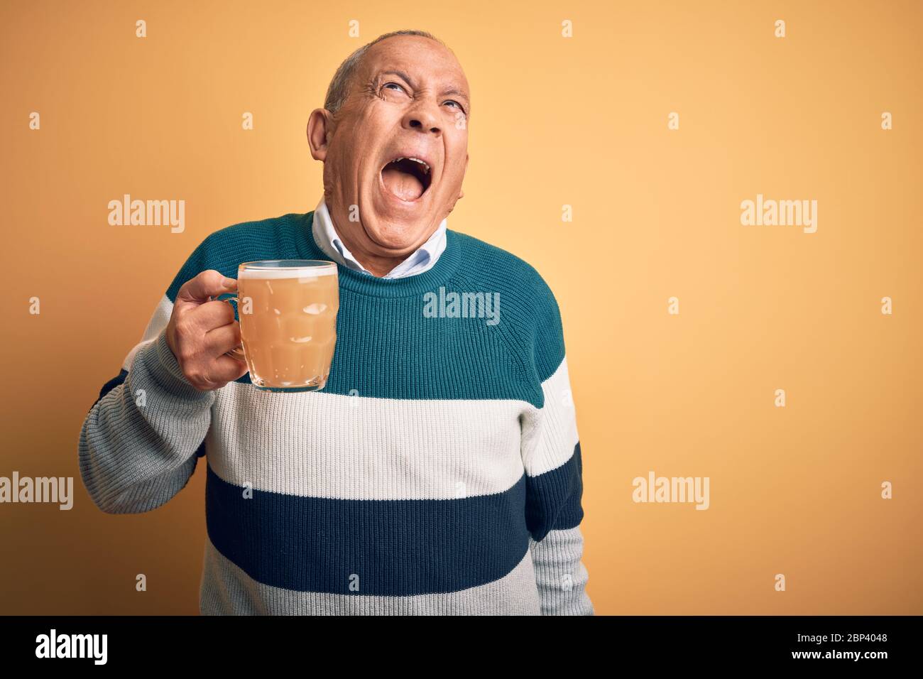 Senior handsome man drinking jar of beer standing over isolated yellow ...