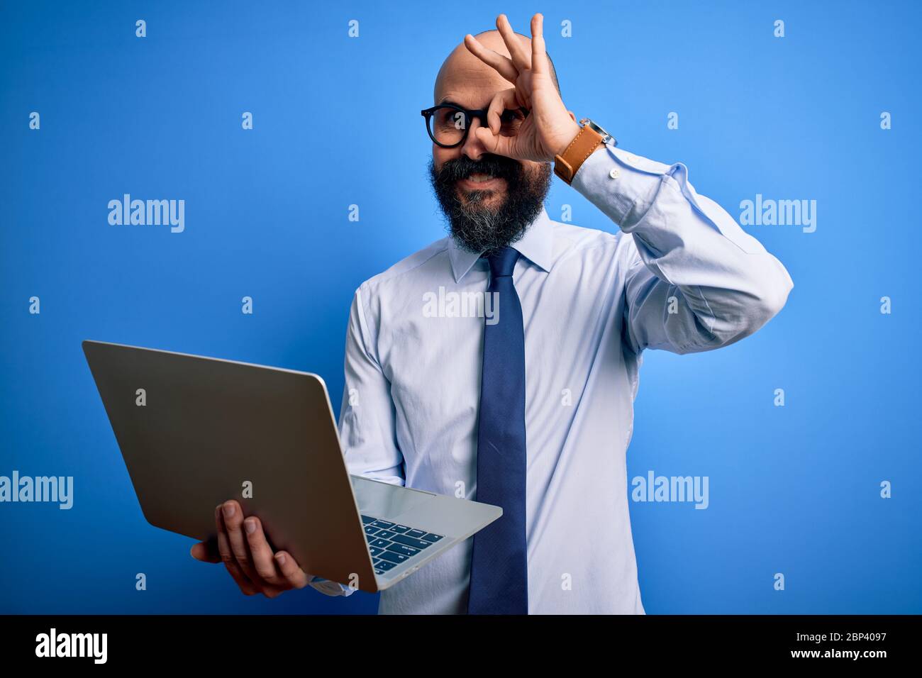 Handsome bald business man with beard working using laptop over blue ...