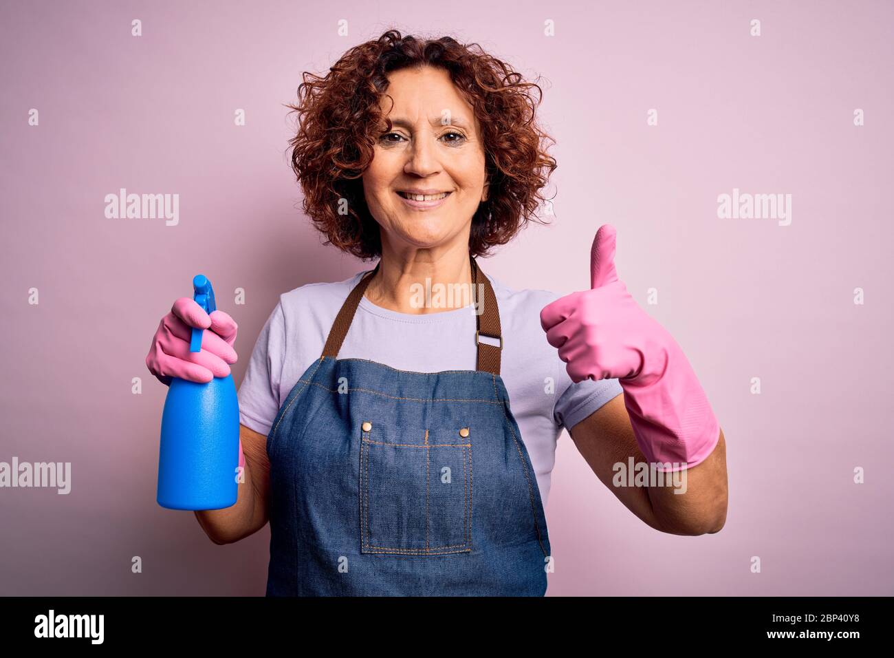 Middle age curly hair woman cleaning doing housework wearing apron and ...