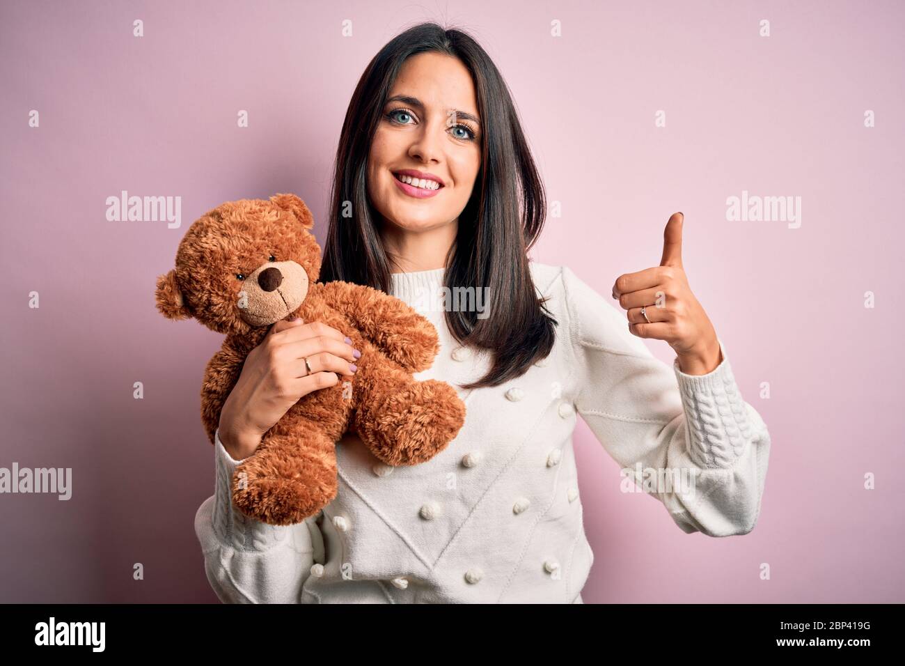 Young brunette woman with blue eyes hugging teddy bear stuffed animal ...
