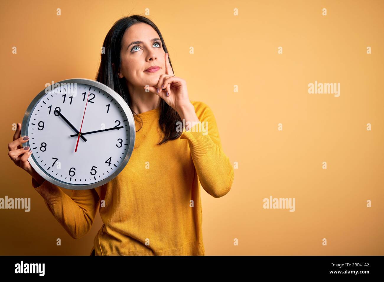 Young woman with blue eyes doing countdown holding big clock over ...