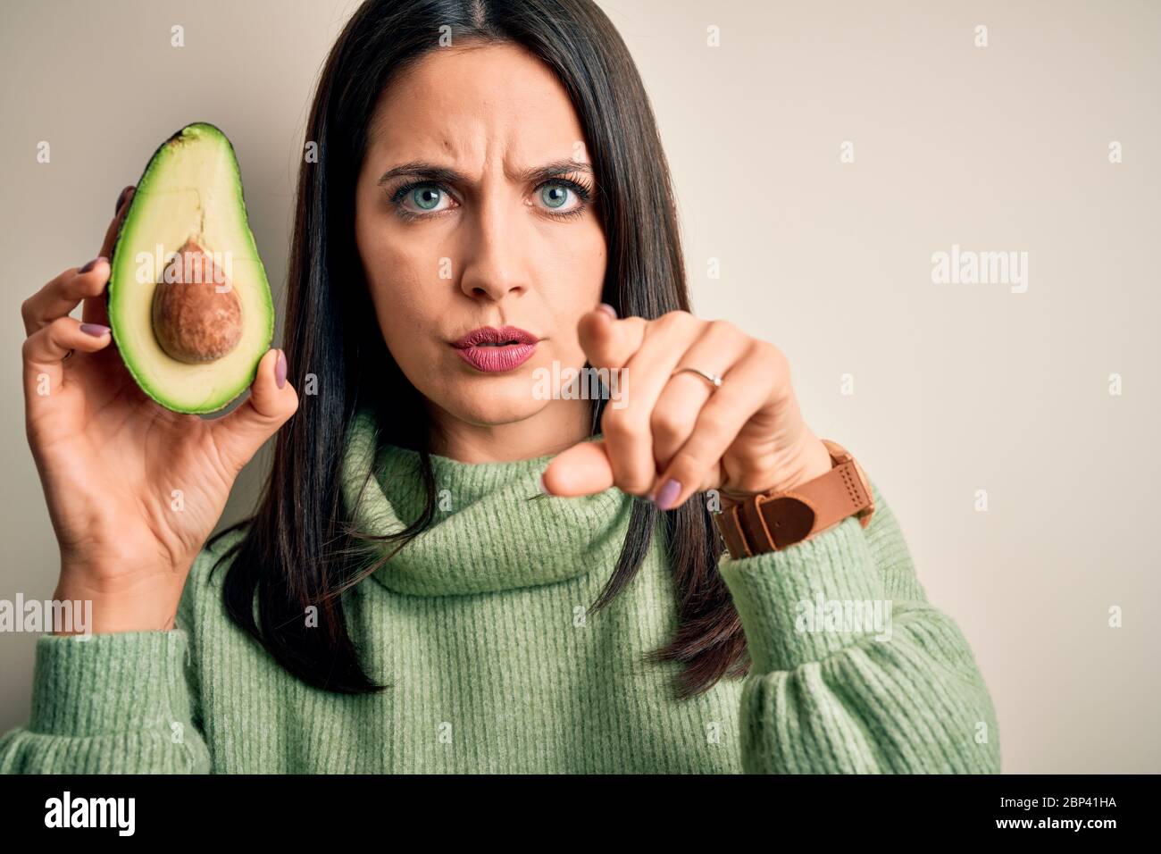 Young woman with blue eyes holding middle healthy avocado over isolated ...