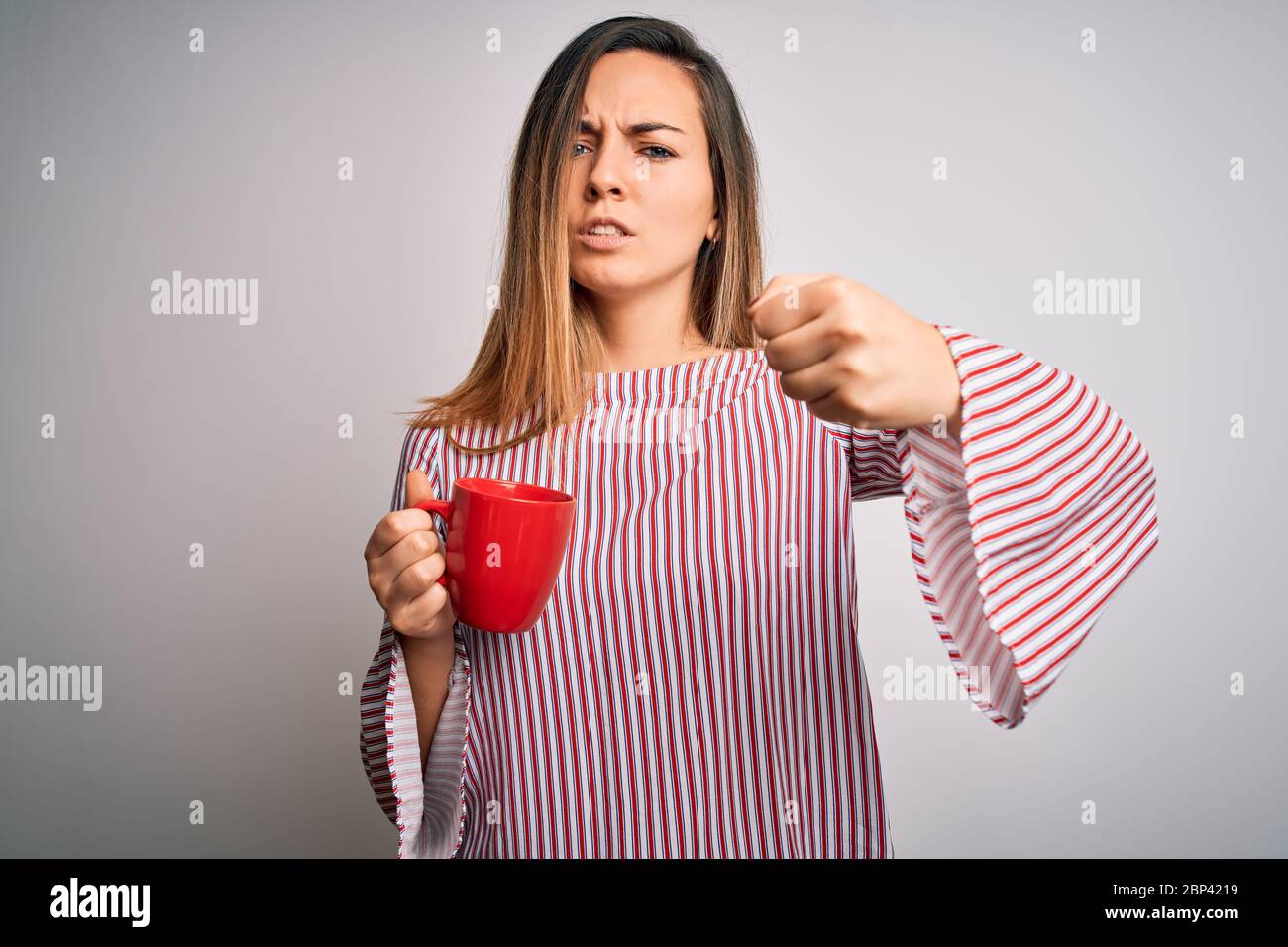 Beautiful blonde woman with blue eyes drinking red mug of coffee over ...