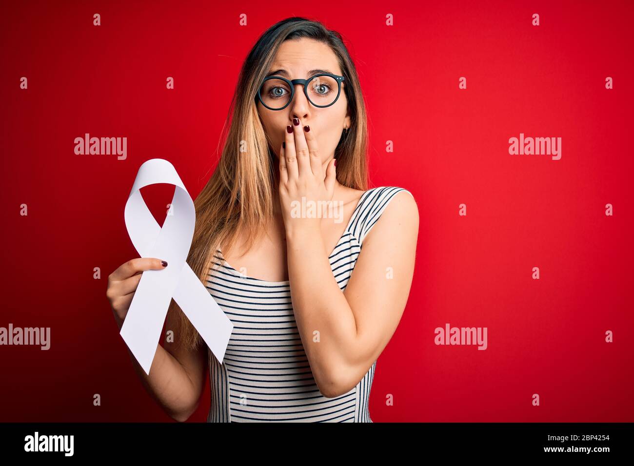 Young beautiful blonde woman with blue eyes holding white ribbon over ...