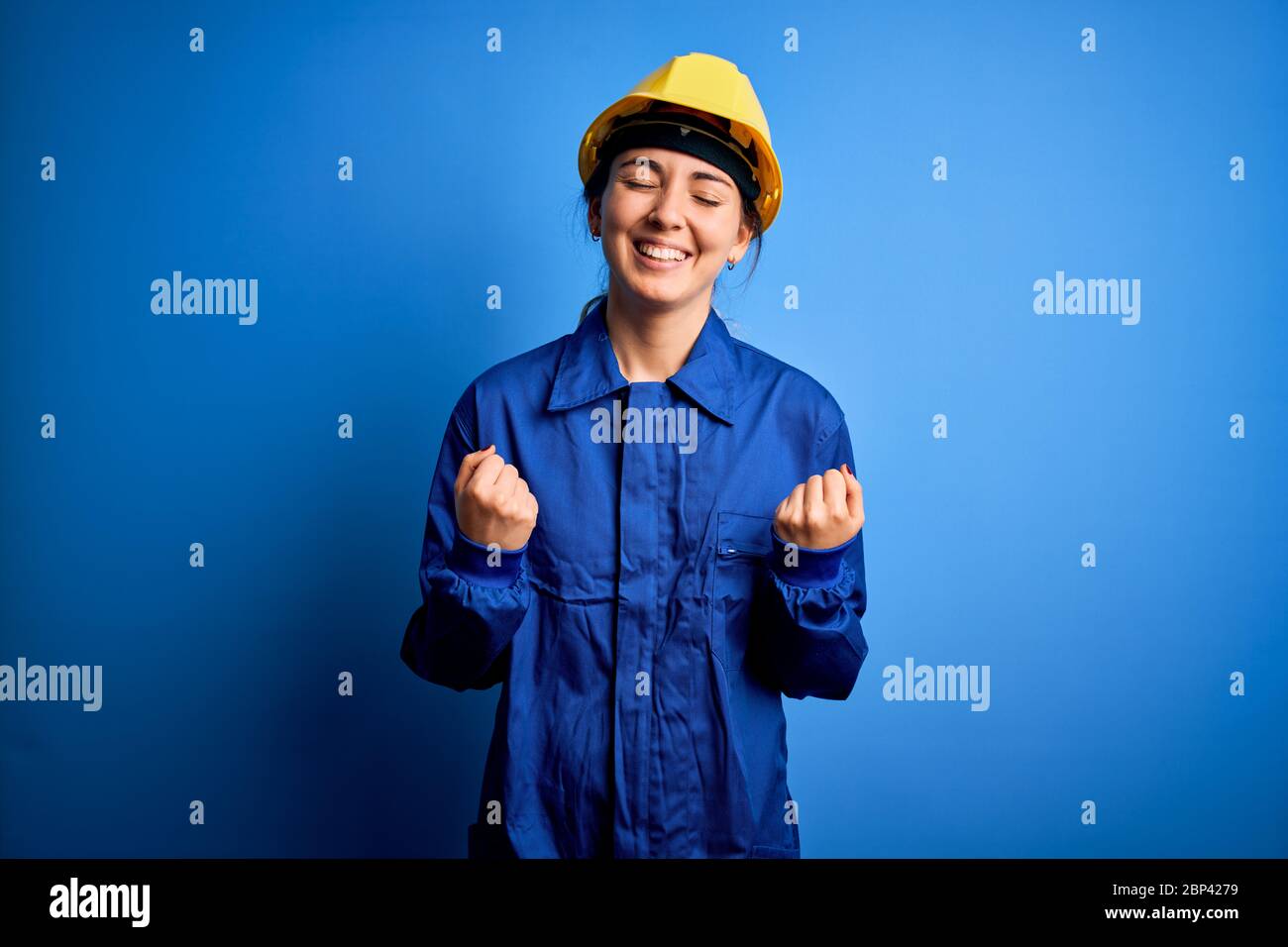 Young beautiful worker woman with blue eyes wearing security helmet and ...