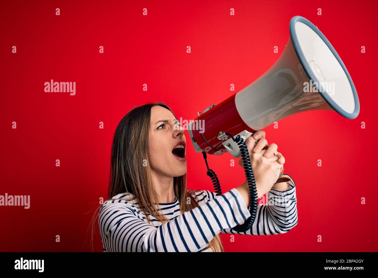 Young caucasian woman shouting on protest through megaphone. Yelling ...