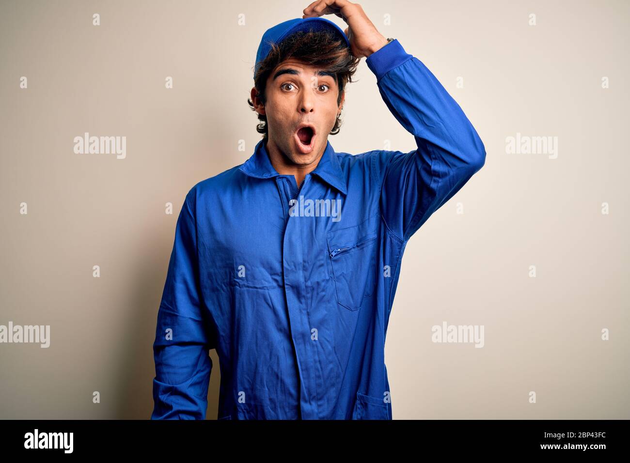 Young mechanic man wearing blue cap and uniform standing over isolated ...