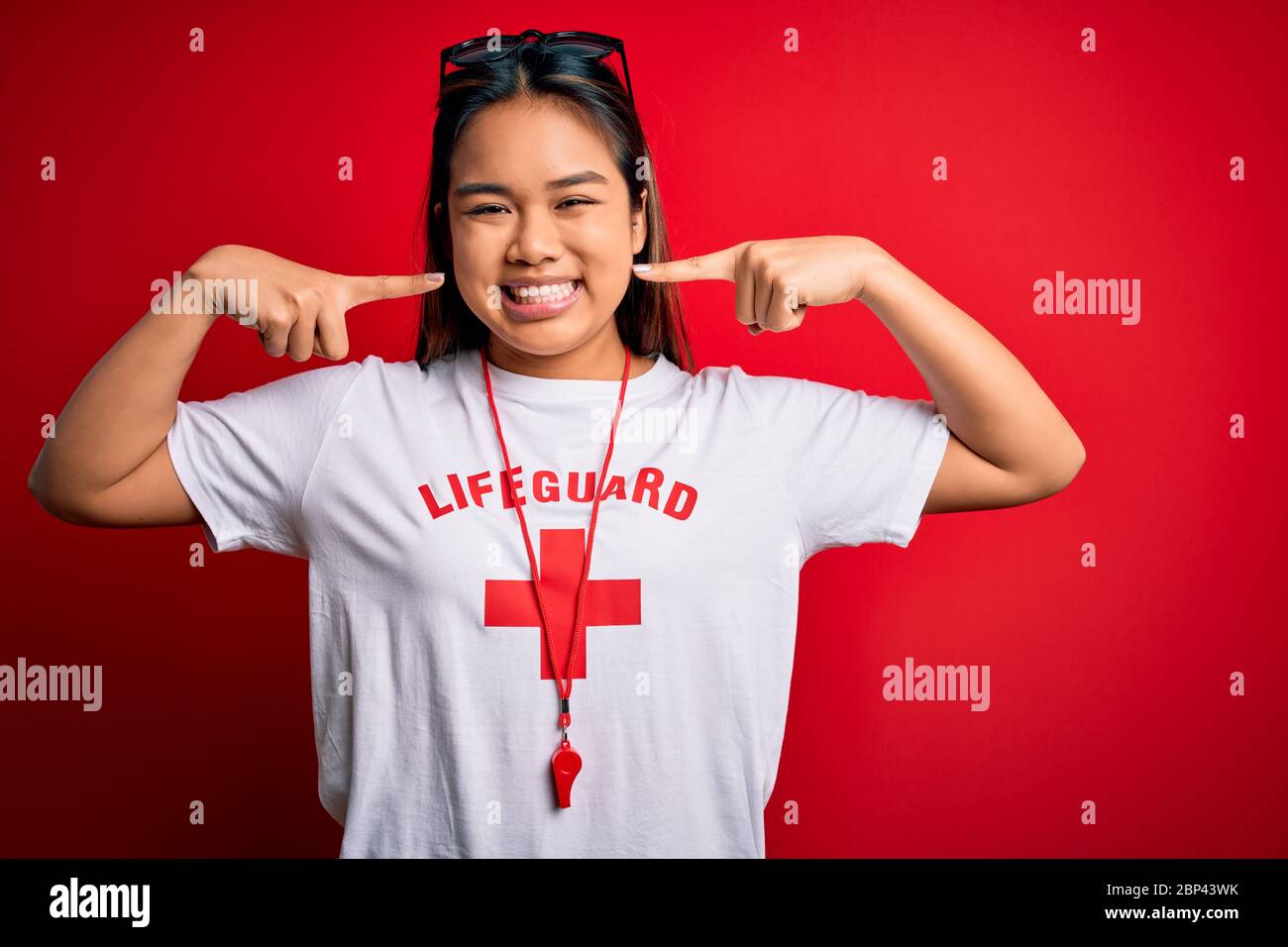 Young asian lifeguard girl wearing t-shirt with red cross using whistle ...