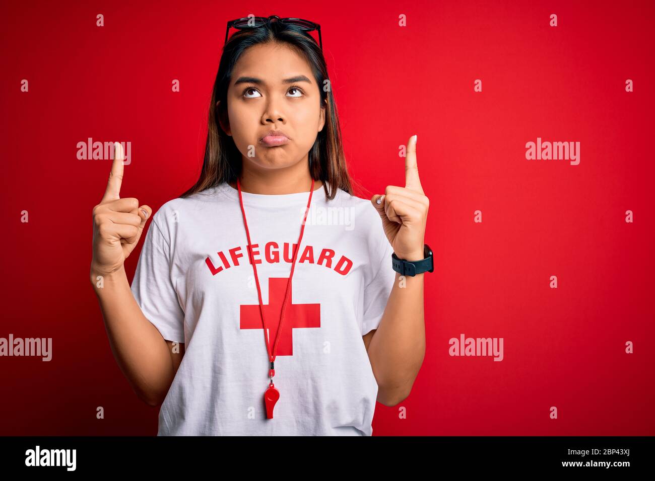Young asian lifeguard girl wearing t-shirt with red cross using whistle ...
