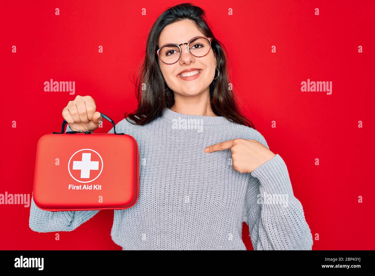 Young beautiful girl holding first aid kit medical box over red ...