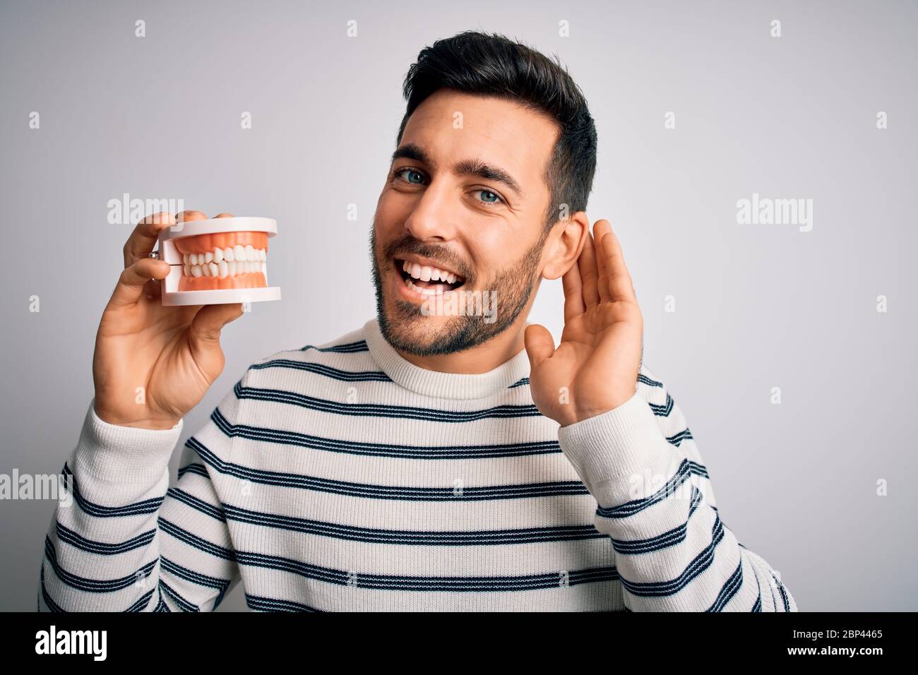 Young handsome man with beard holding plastic denture teeth over white ...