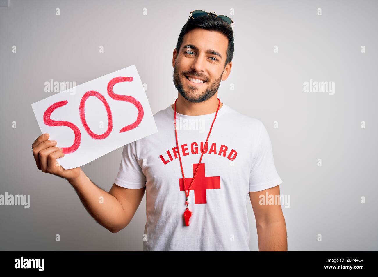 Young lifeguard man with beard wearing whistle holding paper with sos ...