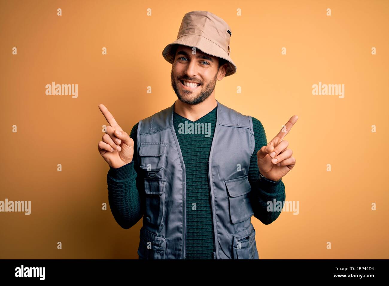 Handsome tourist man with beard on vacation wearing explorer hat over ...