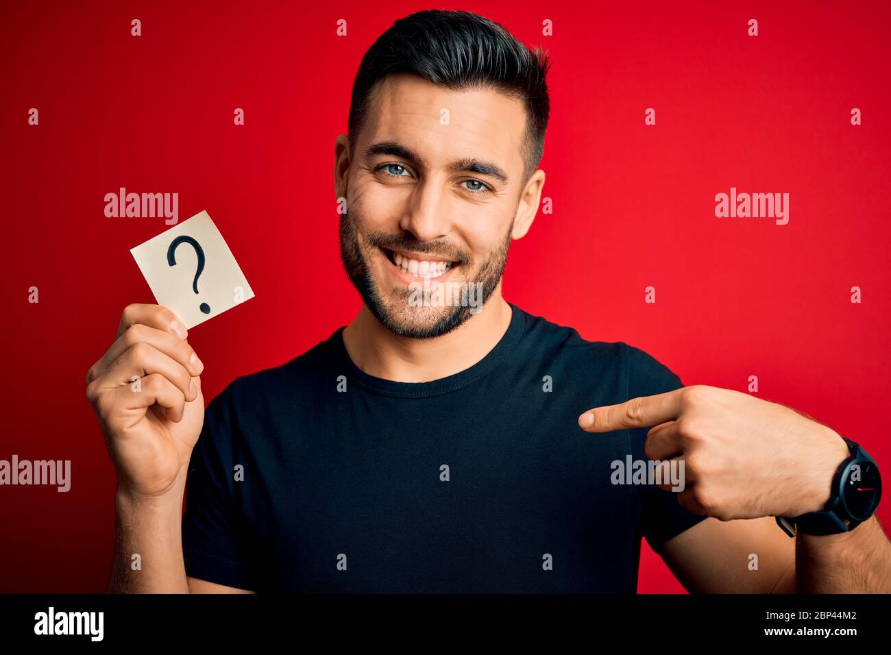 Young handsome man holding paper with question mark symbol over red ...