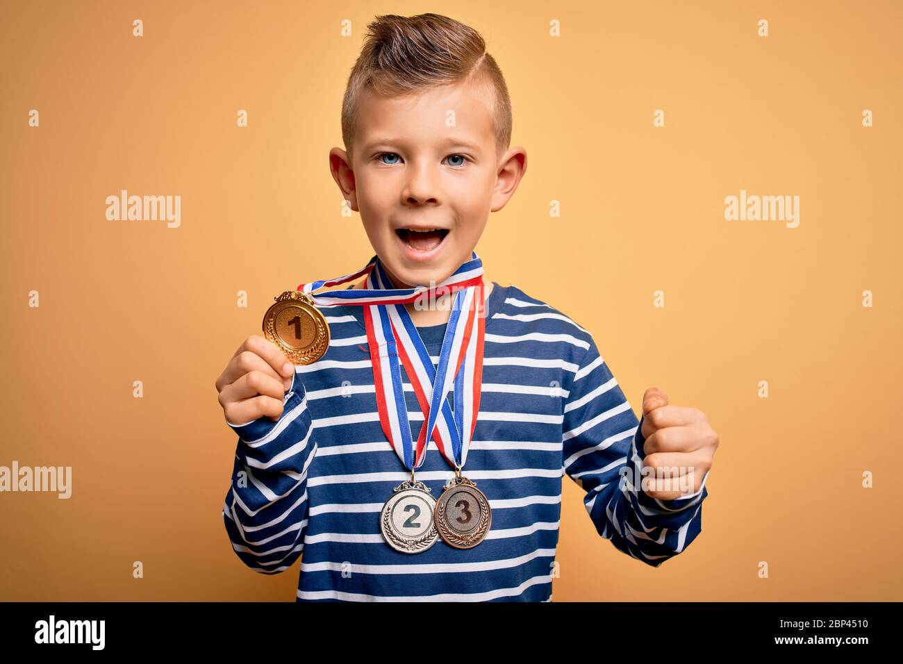 Young little caucasian winner kid wearing award competition medals over ...