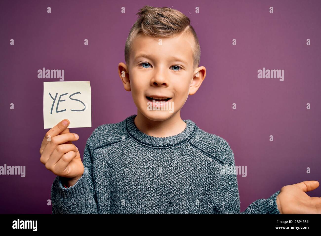 Young little caucasian kid showing YES word on a paper note as positive and success message very ...