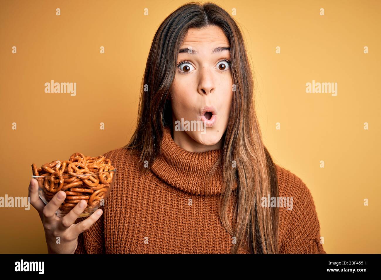 Young beautiful girl eating baked german pretzel standing over isolated ...