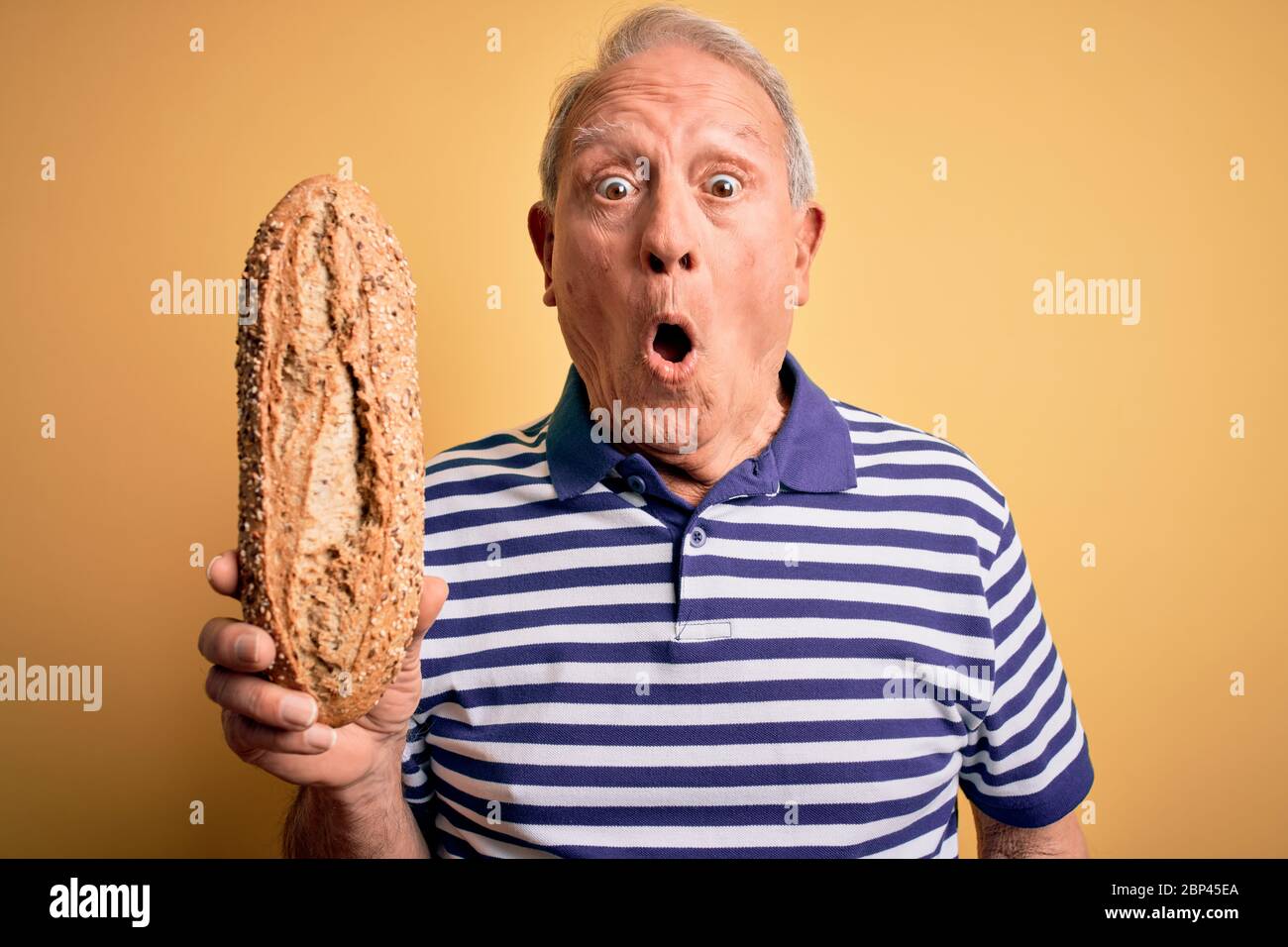 Grey haired senior man holding healthy wholemeal bread over yellow ...