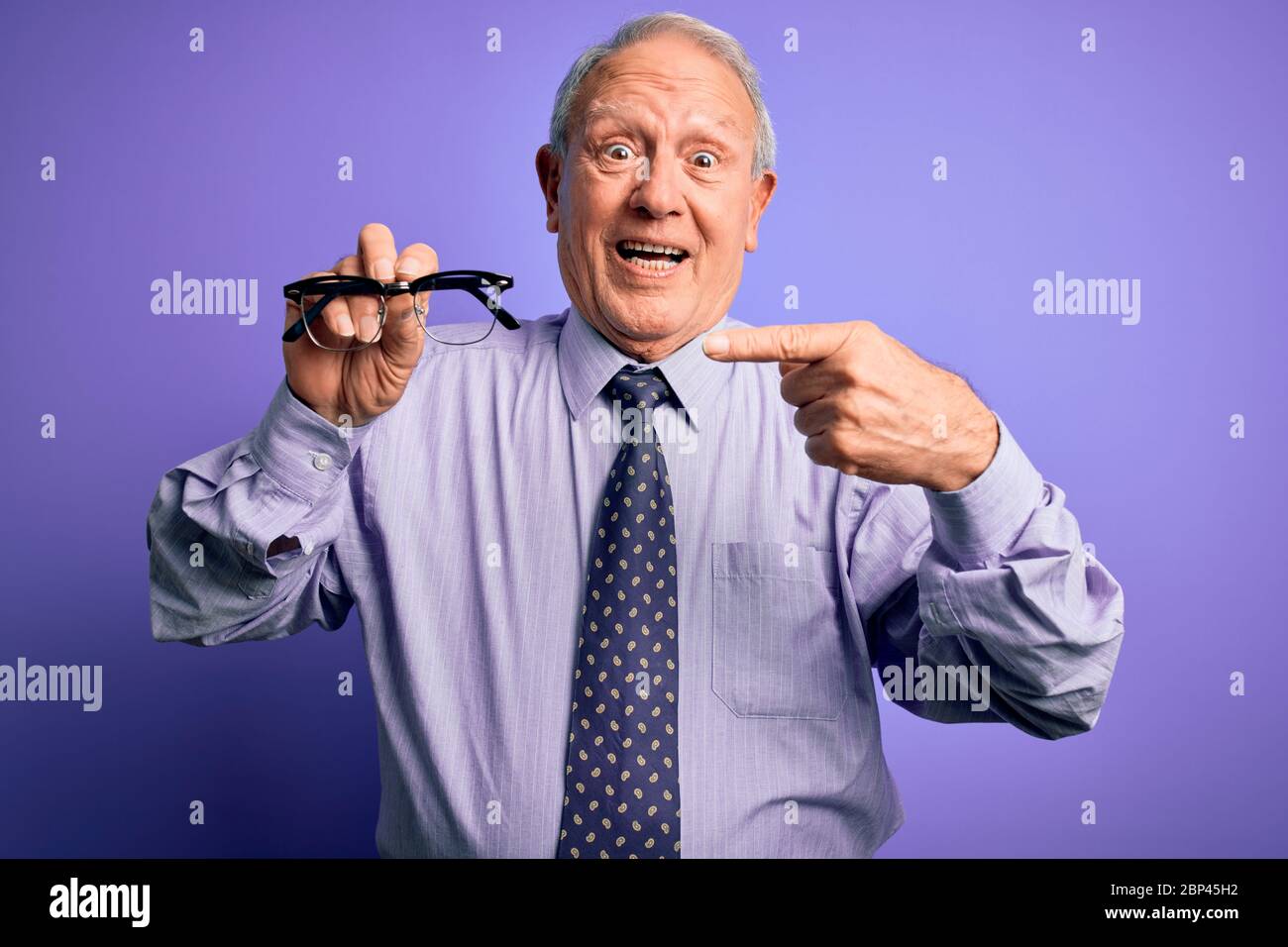 Senior grey haired man holding correction glasses over purple ...