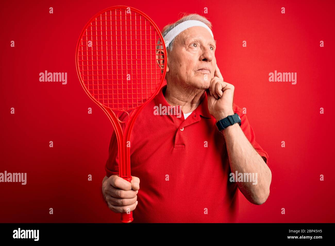Grey haired senior tennis player man holding racket over red isolated ...