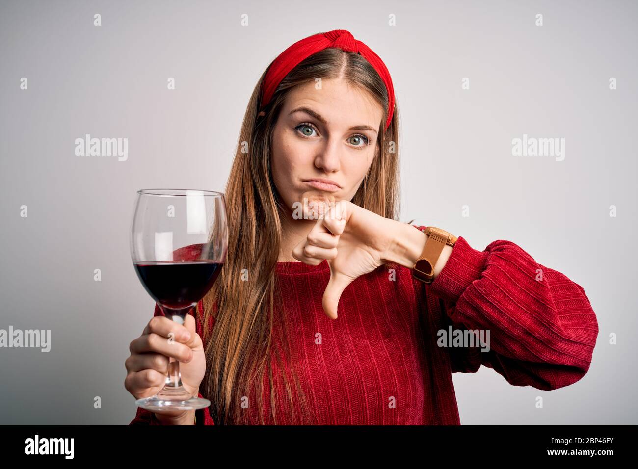 Young beautiful redhead woman drinking glass of red wine over isolated ...