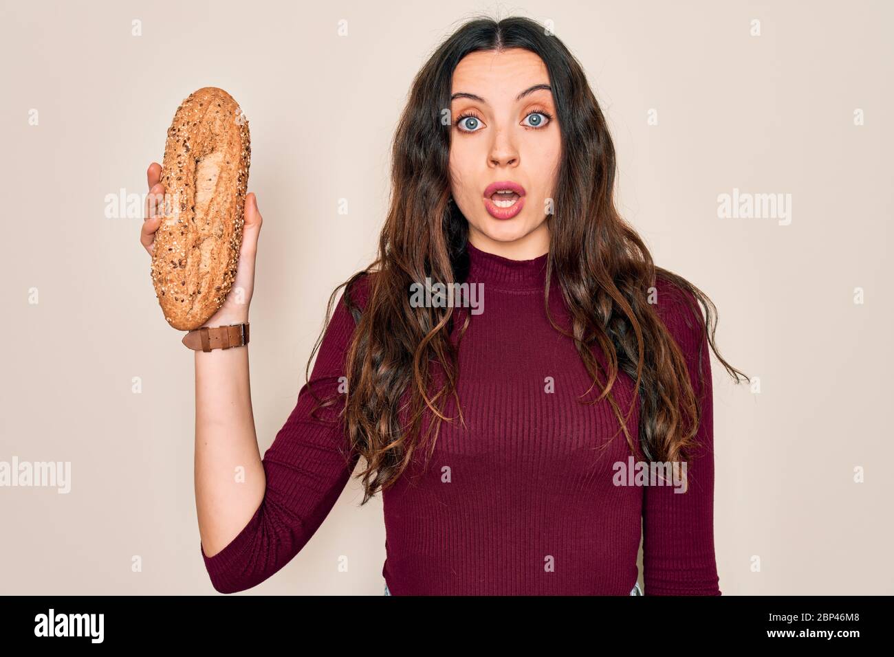 Young beautiful woman holding wholemeal bread cereal over isolated ...
