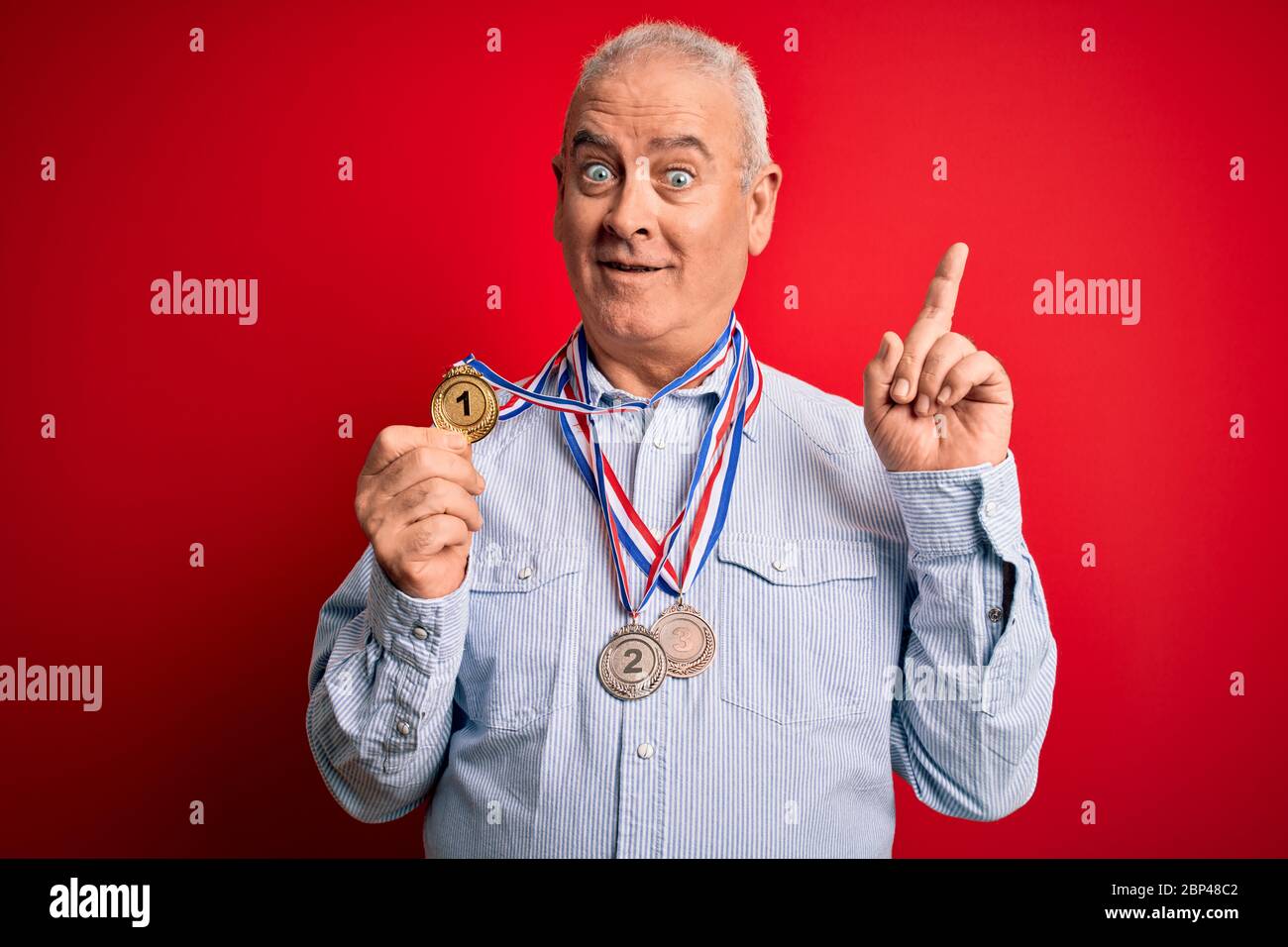 Middle age hoary champion man wearing medals standing over isolated red ...