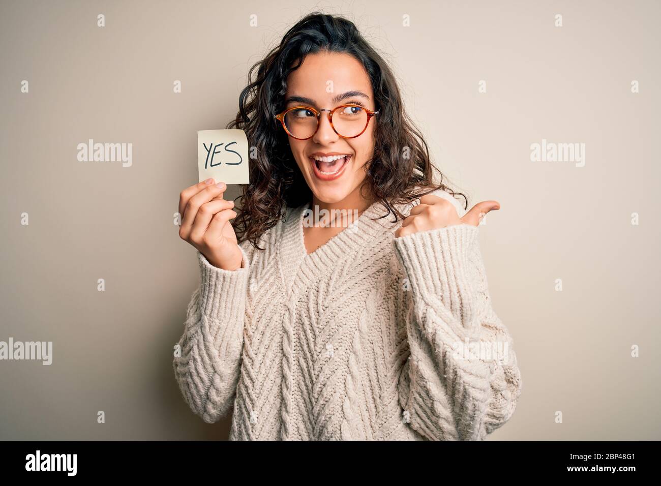 Young beautiful woman with curly hair holding reminder paper with yes ...