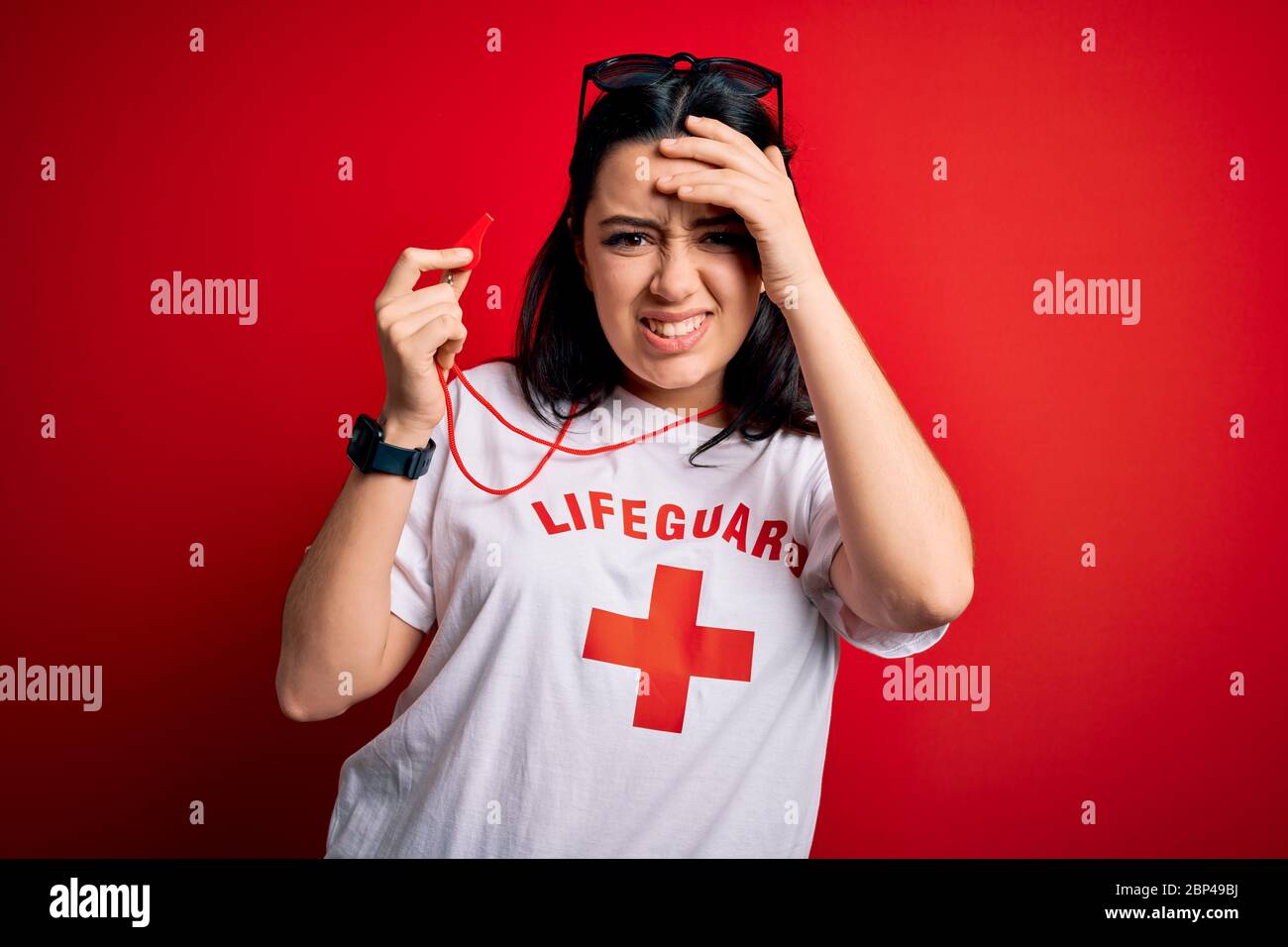 Young lifeguard woman wearing guard equipement holding whistle over red ...
