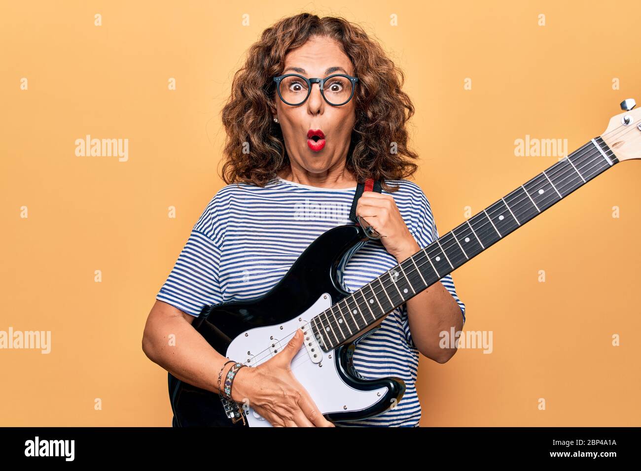 Middle age beautiful musician woman playing electric guitar over ...