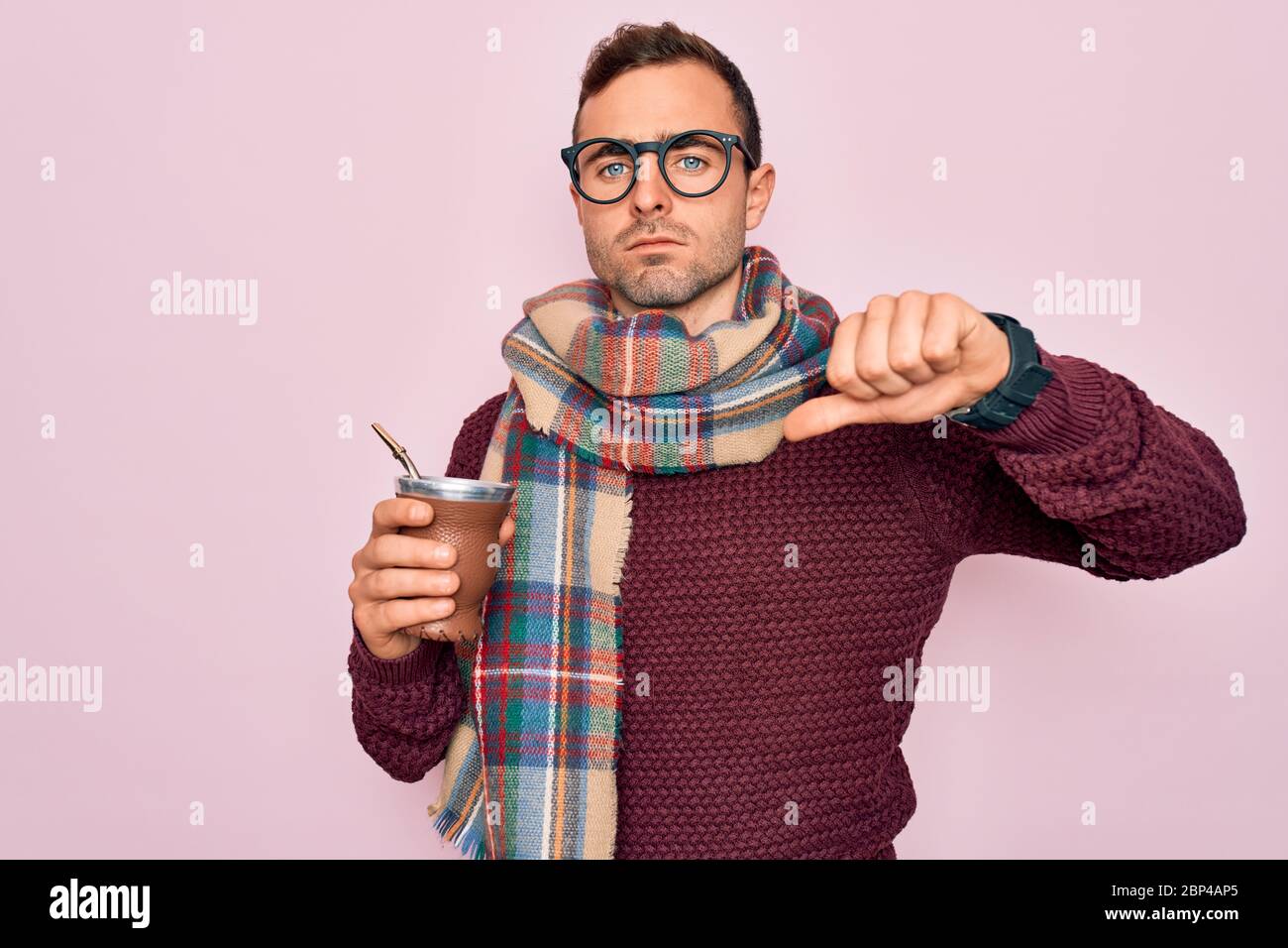 Young handsome man with blue eyes drinking cup of hot mate tea over ...
