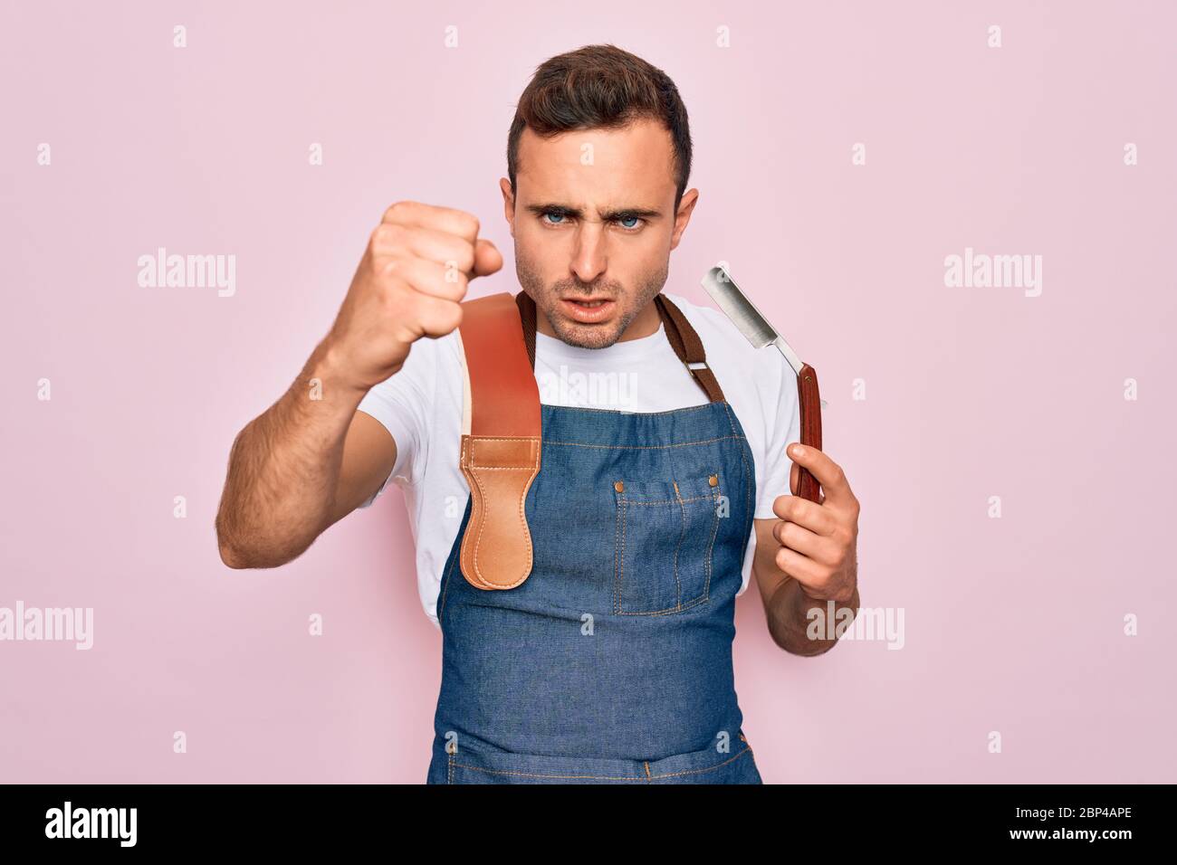 Handsome barber man with blue eyes wearing apron using razor blade over ...
