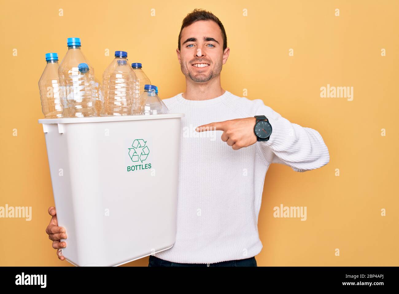 Young handsome man with blue eyes recycling holding wastebasket with ...