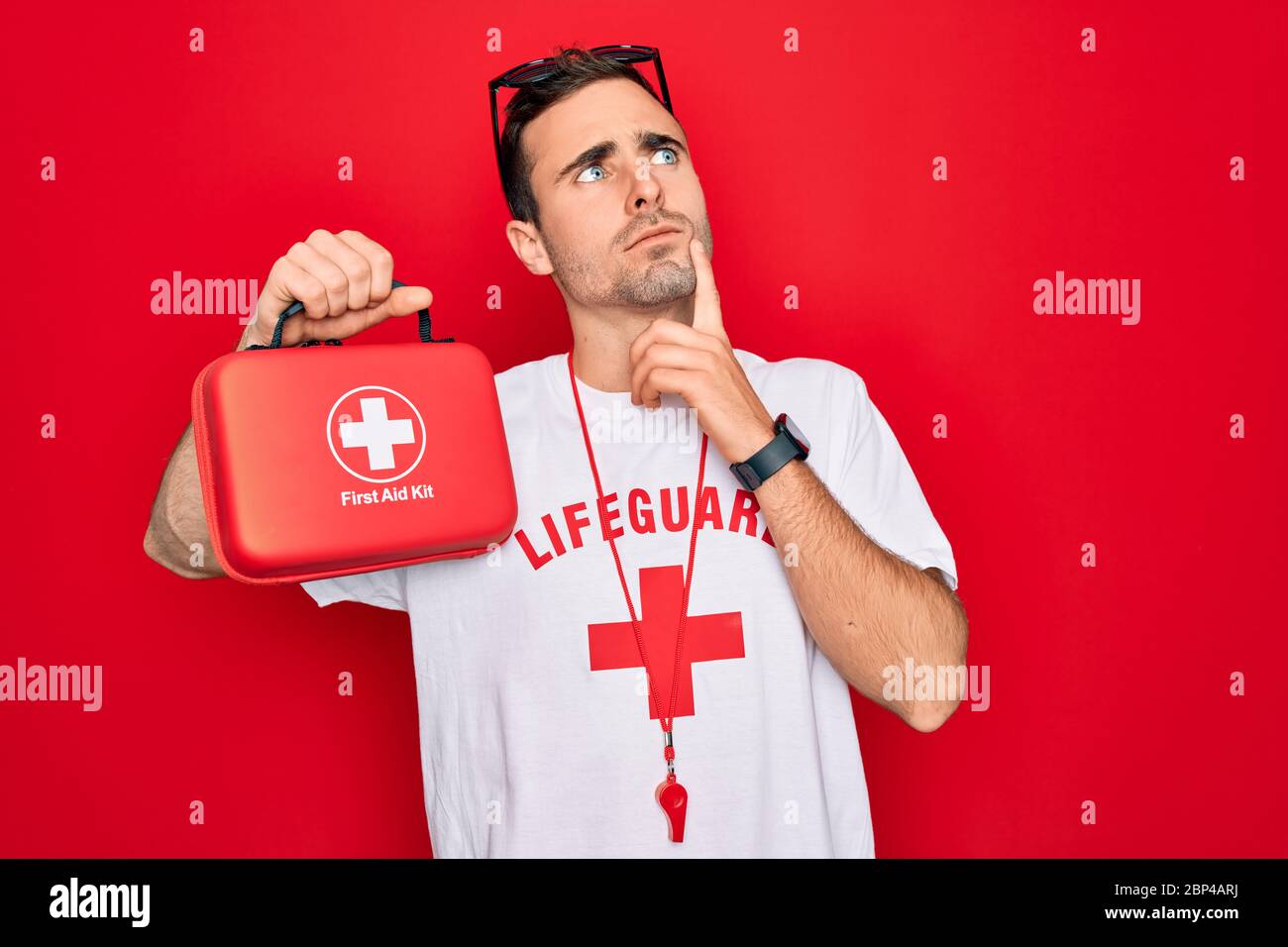 Young handsome lifeguard man wearing t-shirt with red cross and whistle ...