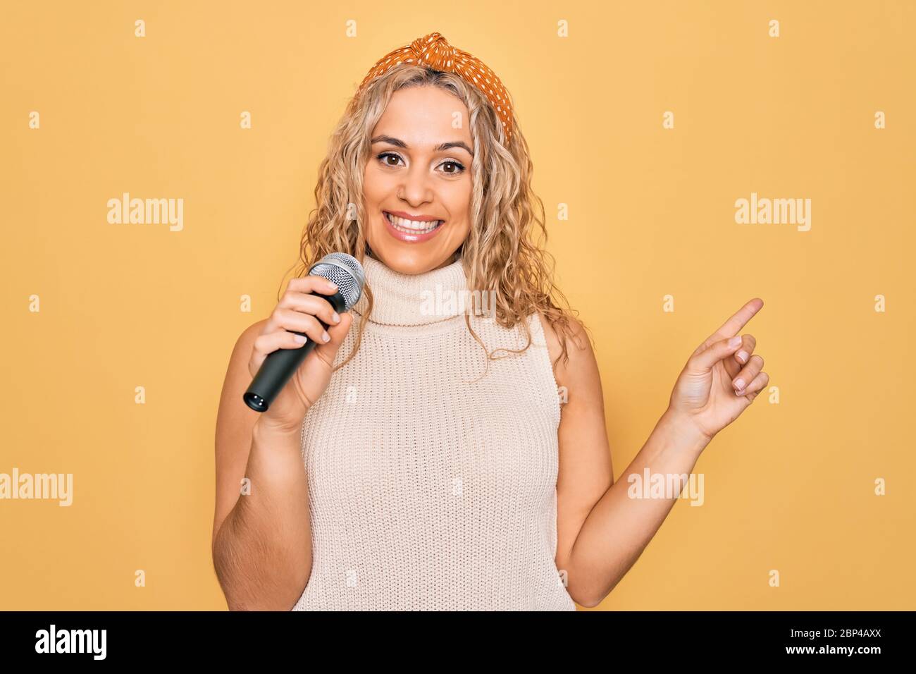 Young beautiful blonde singer woman singing using microphone over ...