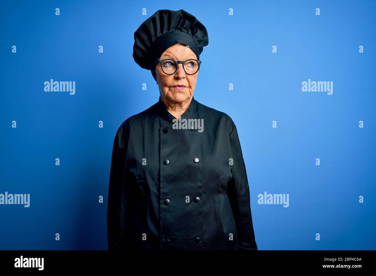 Senior beautiful grey-haired chef woman wearing cooker uniform and hat ...