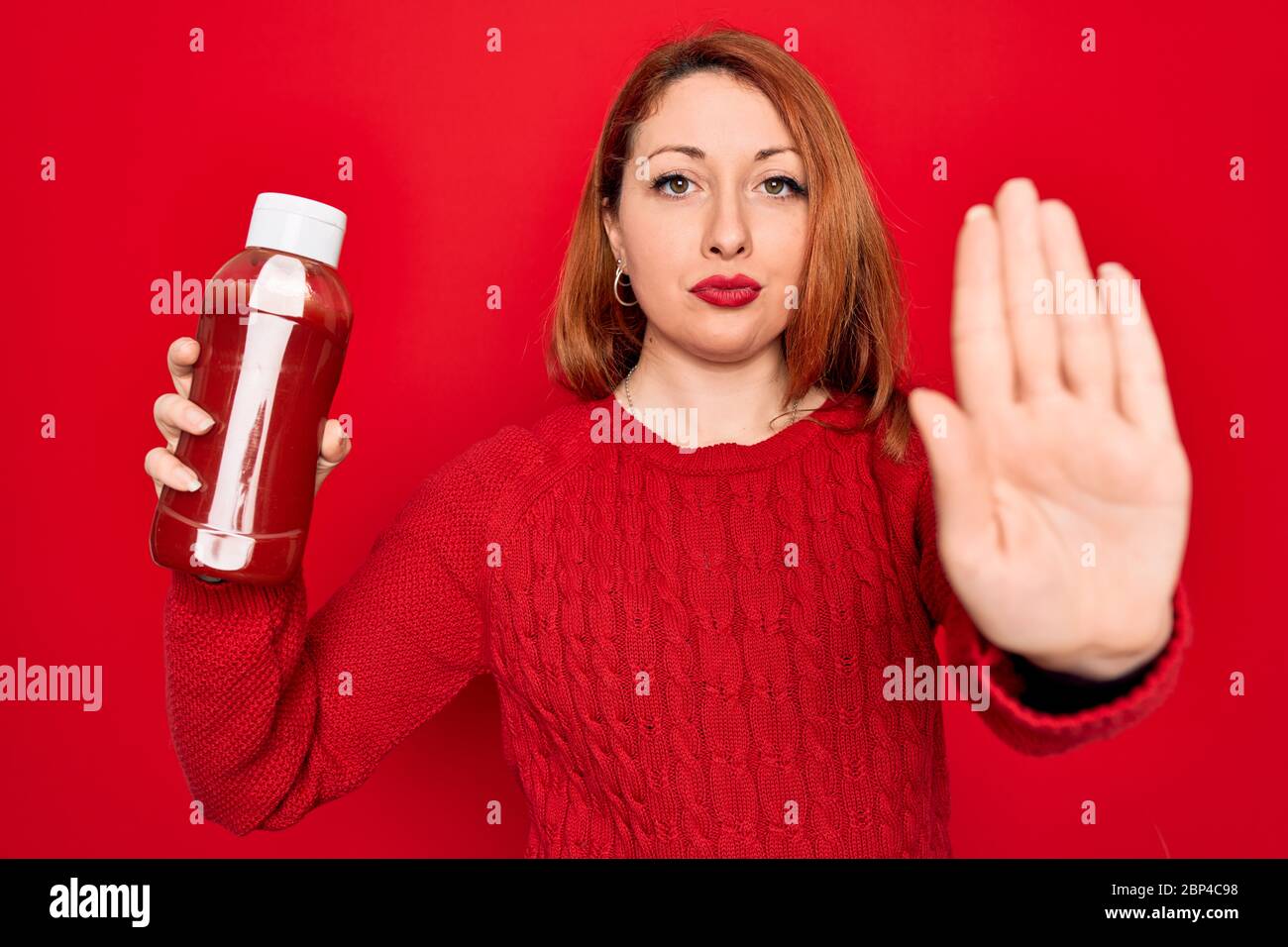 Beautiful redhead woman holding bottle of ketchup sauce condiment over ...