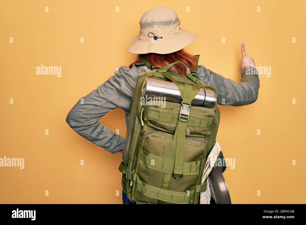 Young redhead backpacker woman hiking wearing backpack and hat over ...